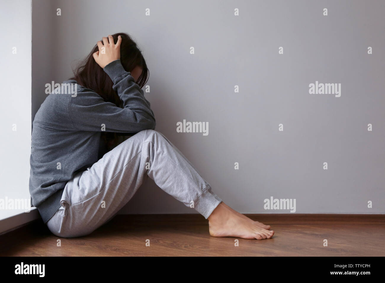 Depressed young woman sitting on floor in empty room Stock Photo - Alamy