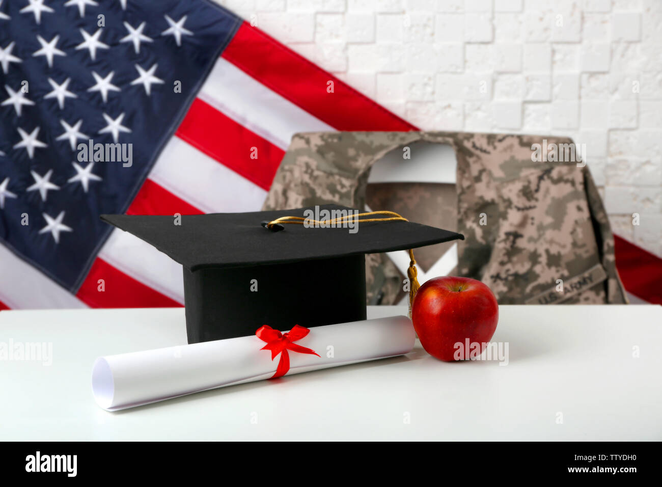 Graduation hat, apple and diploma on white table. USA military ...