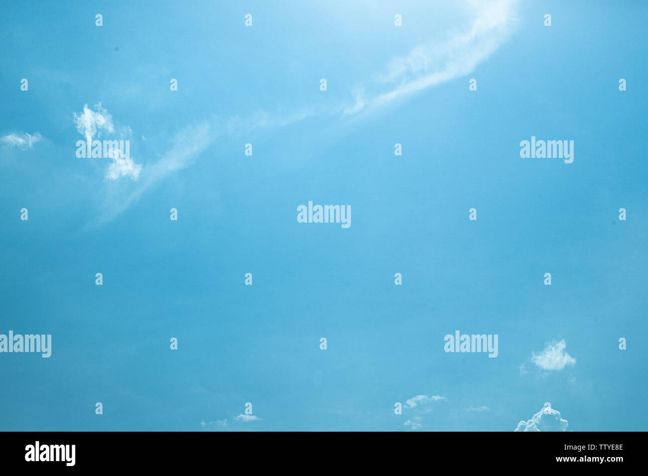 Sunny blue sky with soft clouds and bright sun against green trees ...