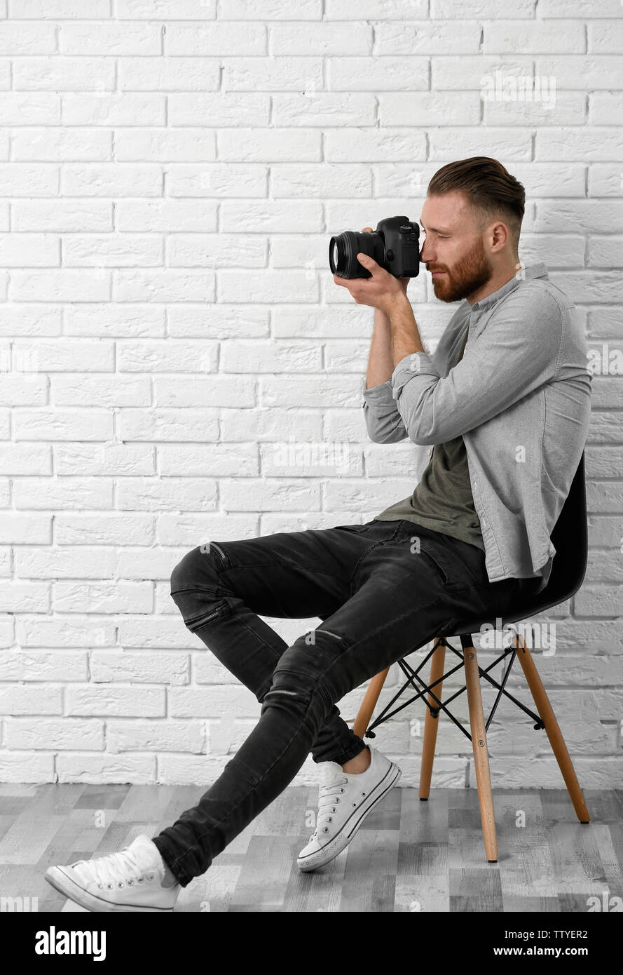 Handsome photographer sitting on chair near light brick wall Stock ...