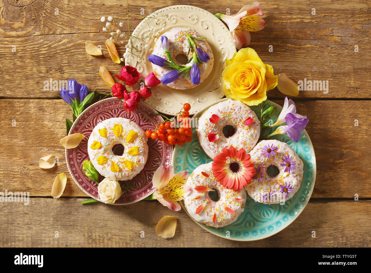 Composition of plates with delicious donuts and colourful flowers on ...