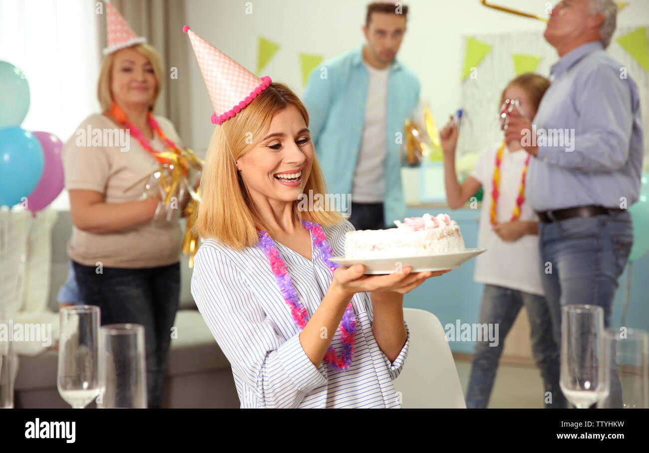 Birthday party. Mother with cake sitting at home with blurred family on ...