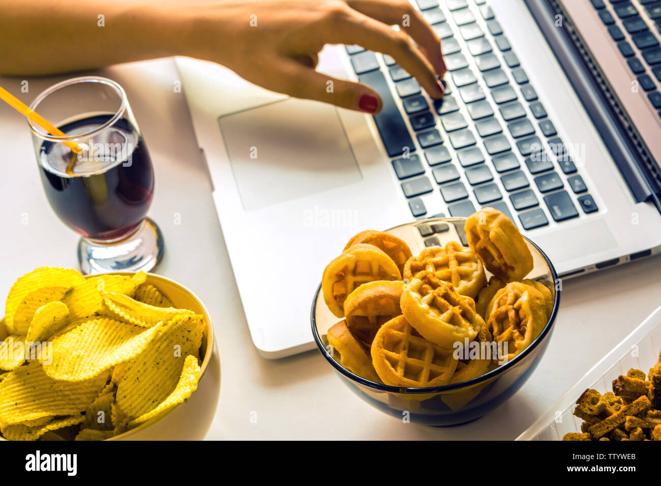 woman hands typing on laptop and unhealthy food: chips, crackers, candy ...