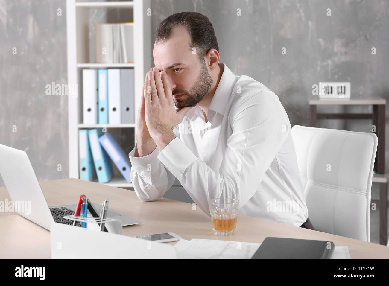 Depressed man sitting in office with glass of whisky Stock Photo - Alamy