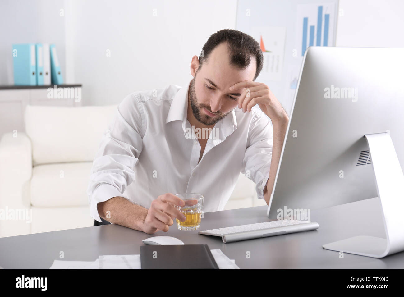 Depressed man sitting in office with glass of whisky Stock Photo - Alamy