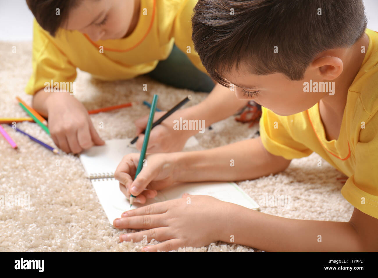 Twin brothers drawing in notebook on floor Stock Photo - Alamy
