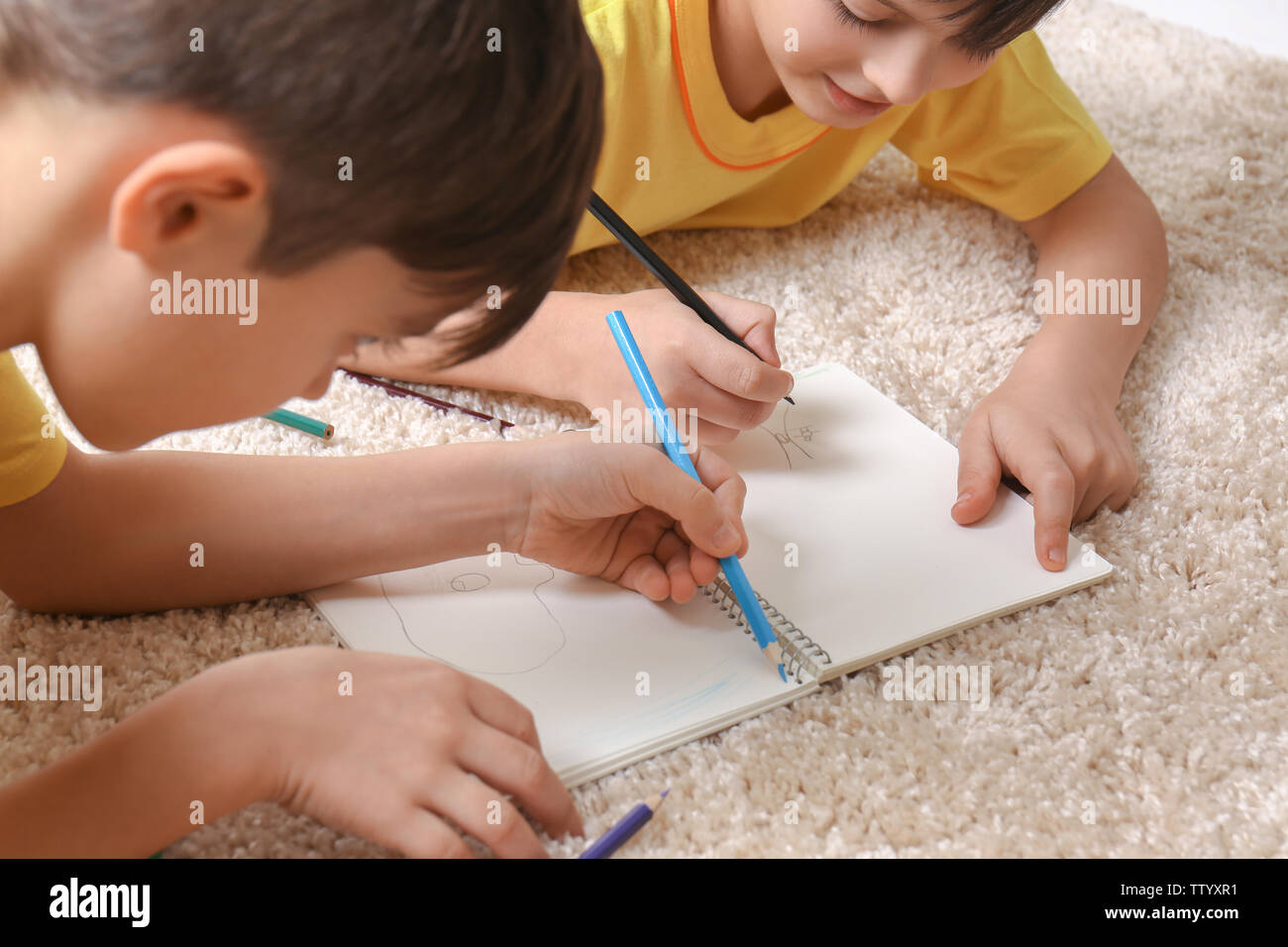 Twin brothers drawing in notebook on floor Stock Photo - Alamy