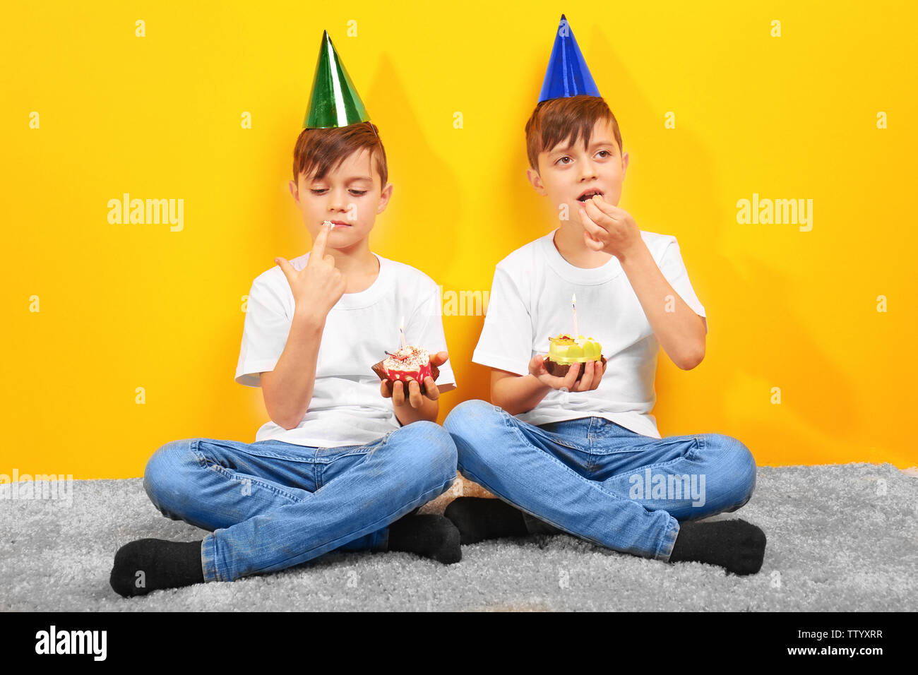 Cute boys with birthday mini cakes on yellow background Stock Photo - Alamy