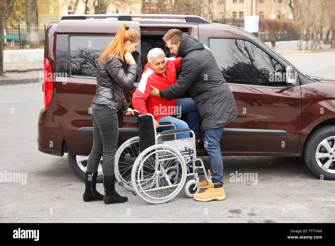 Young couple helping handicapped man to sit in wheelchair Stock Photo ...