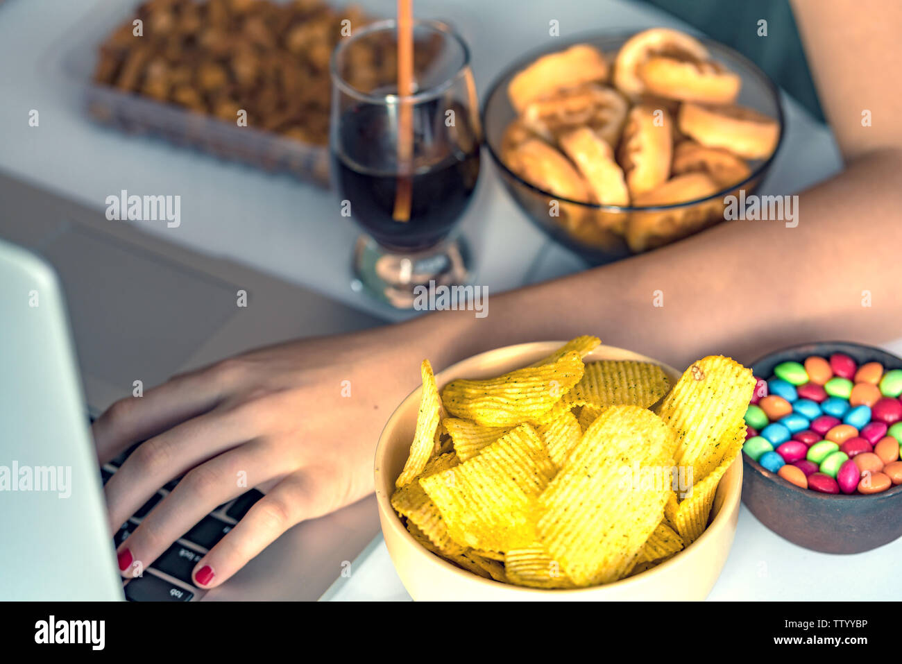 Girl works at a computer and eats fast food. Unhealthy food: chips ...