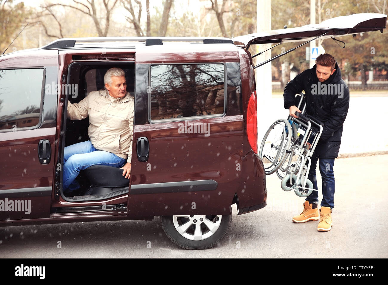 Young man loading wheelchair of handicapped man into car Stock Photo ...