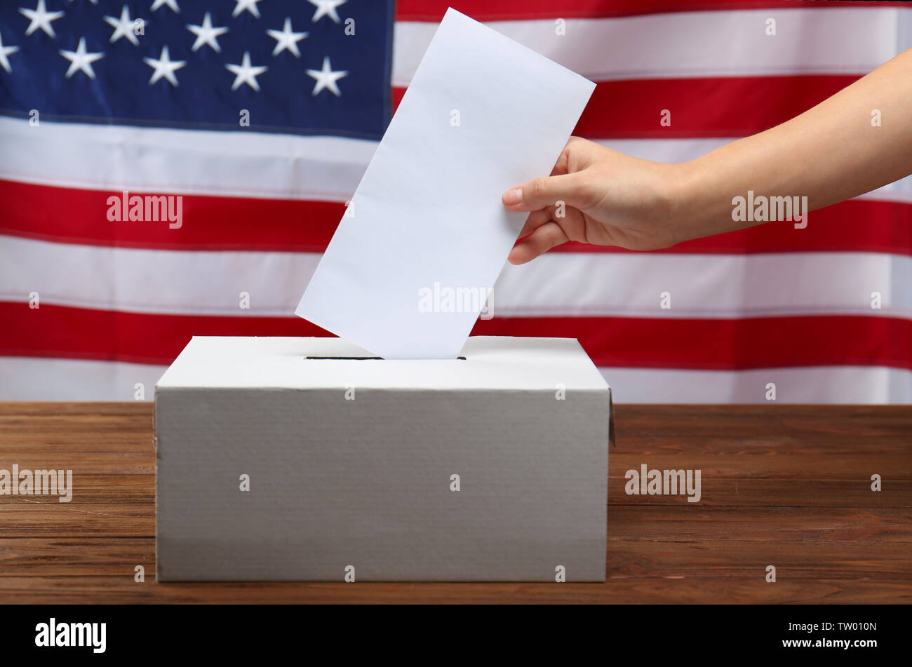 Hand inserting envelope in ballot box on USA national flag background ...