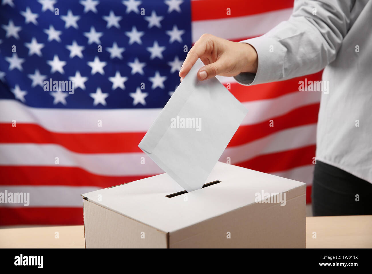 Hand inserting envelope in ballot box on USA national flag background ...