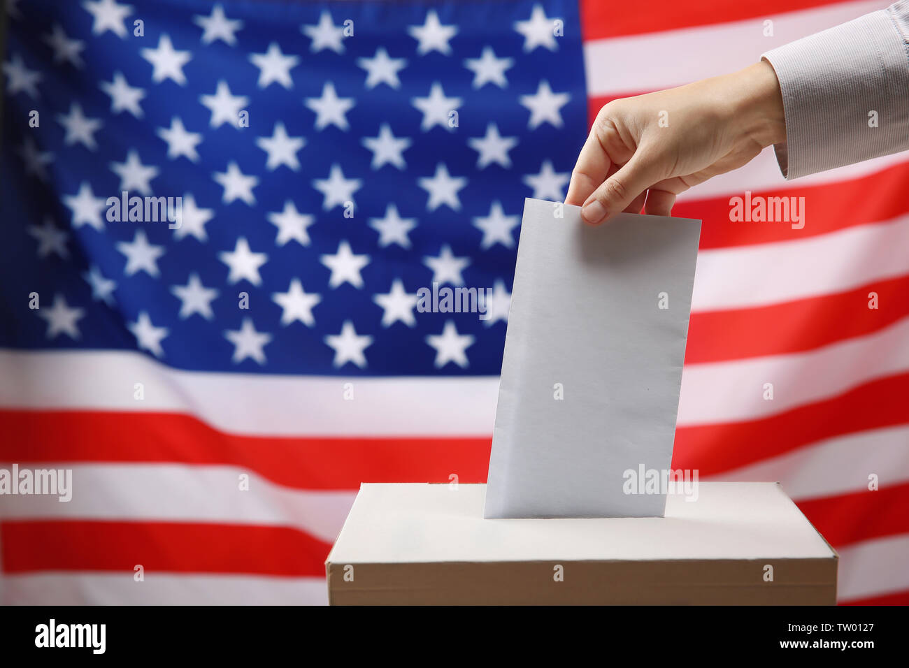 Hand inserting envelope in ballot box on USA national flag background ...