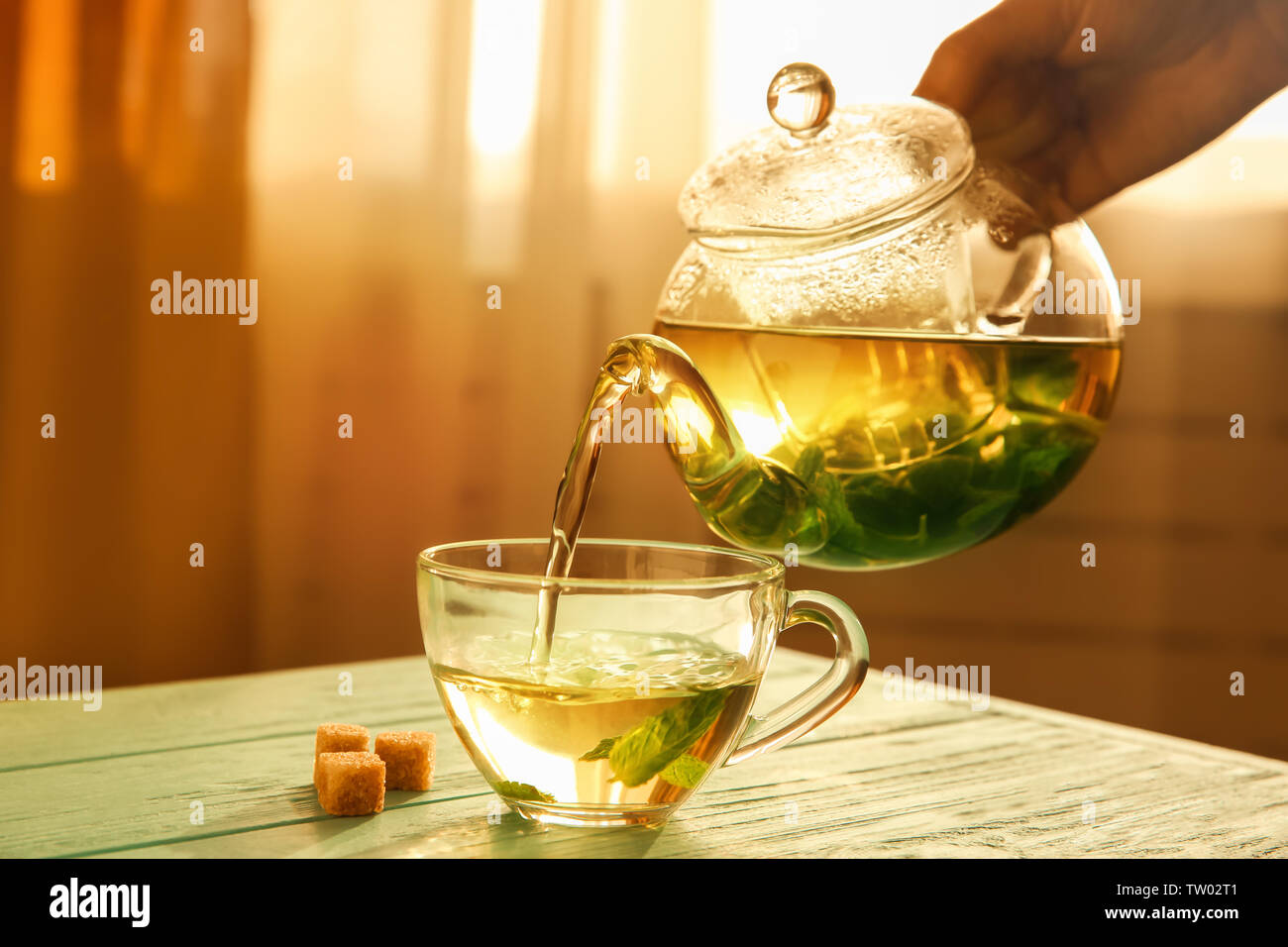 Hand pouring tea from glass teapot into a cup Stock Photo - Alamy