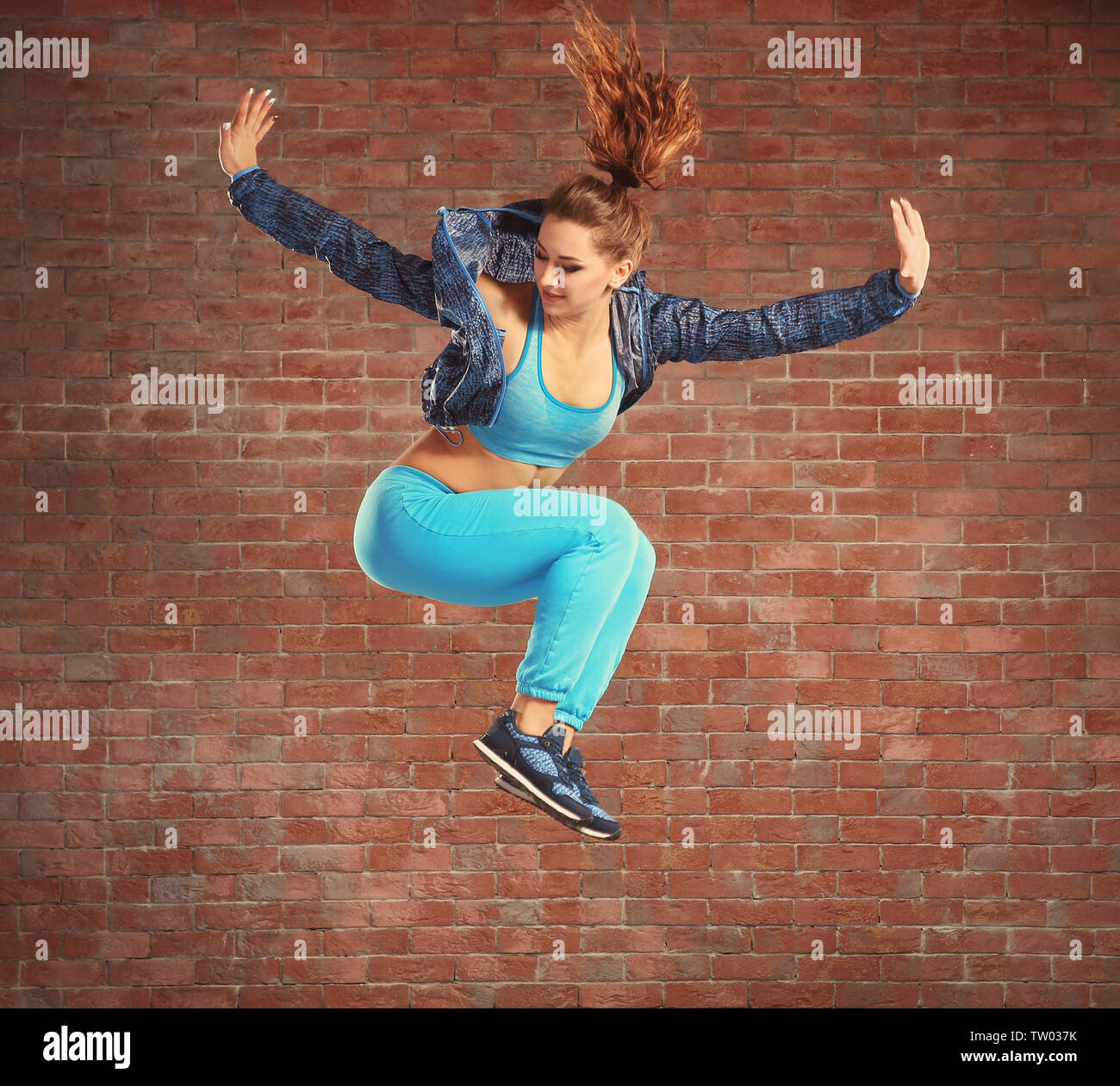 Beautiful young hip-hop dancer jumping against brick wall Stock Photo ...