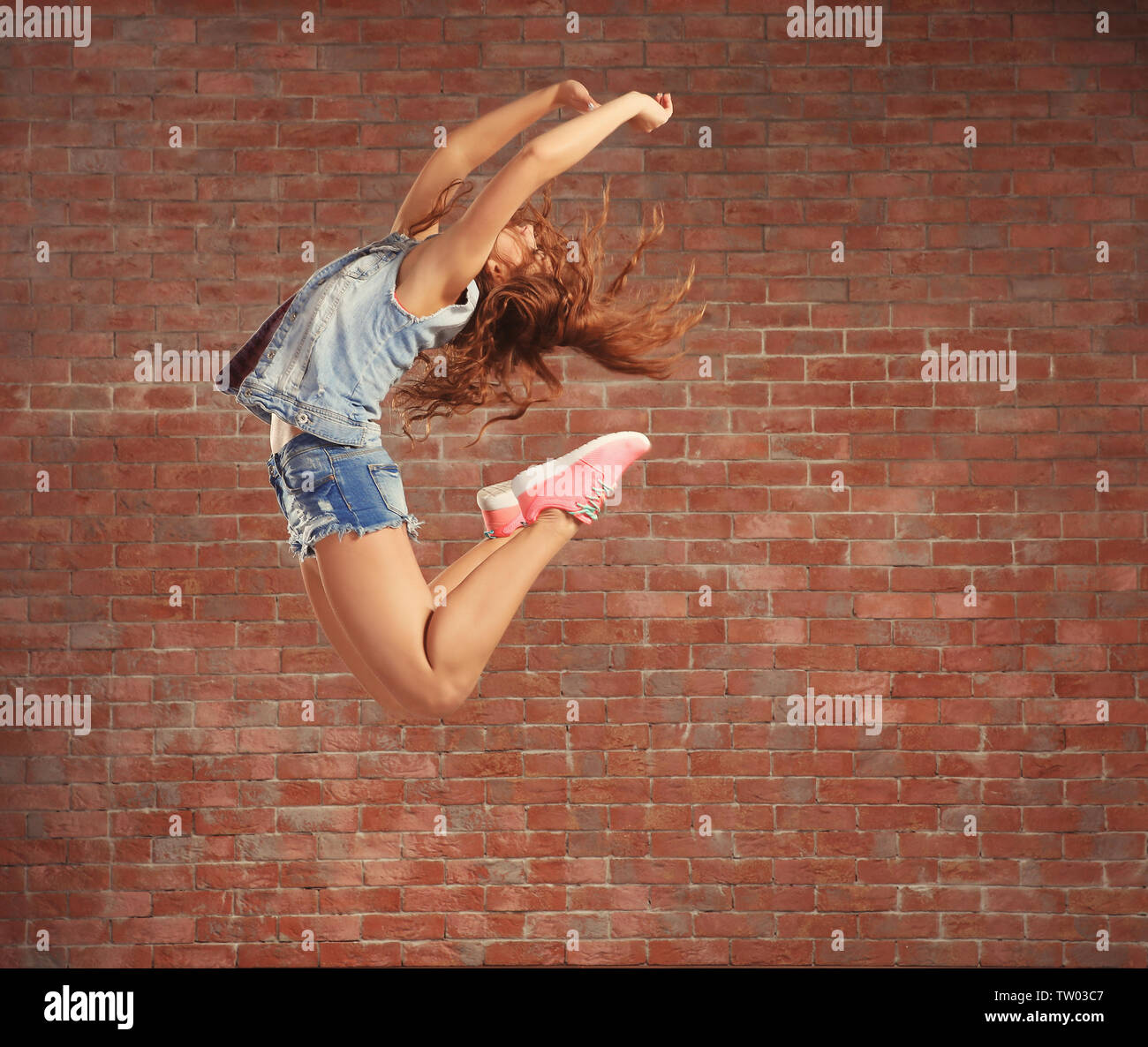 Beautiful young hip-hop dancer jumping against brick wall Stock Photo ...