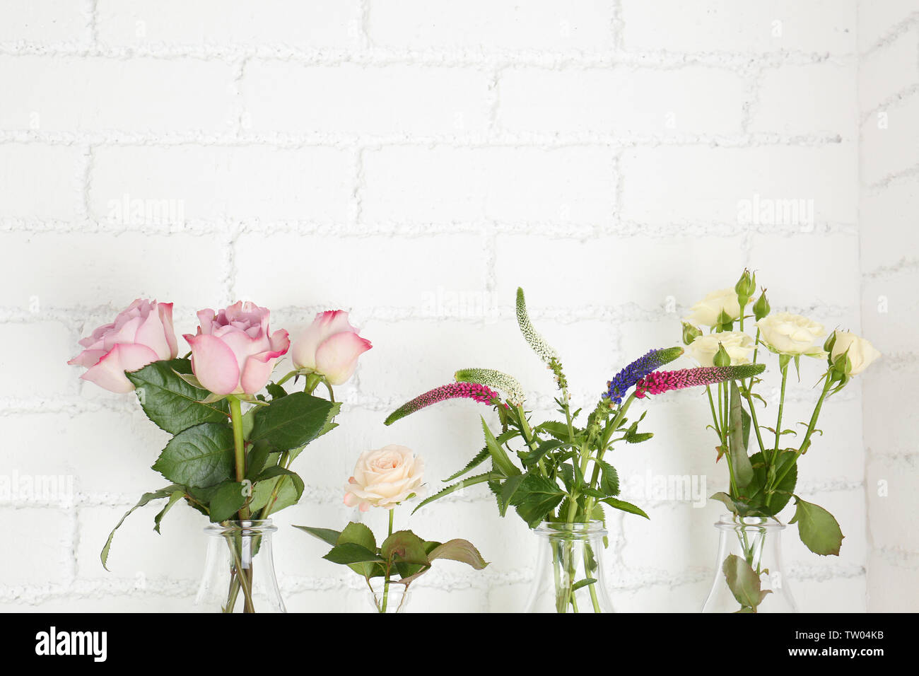 Beautiful flowers in glass vases on brick wall background Stock Photo ...