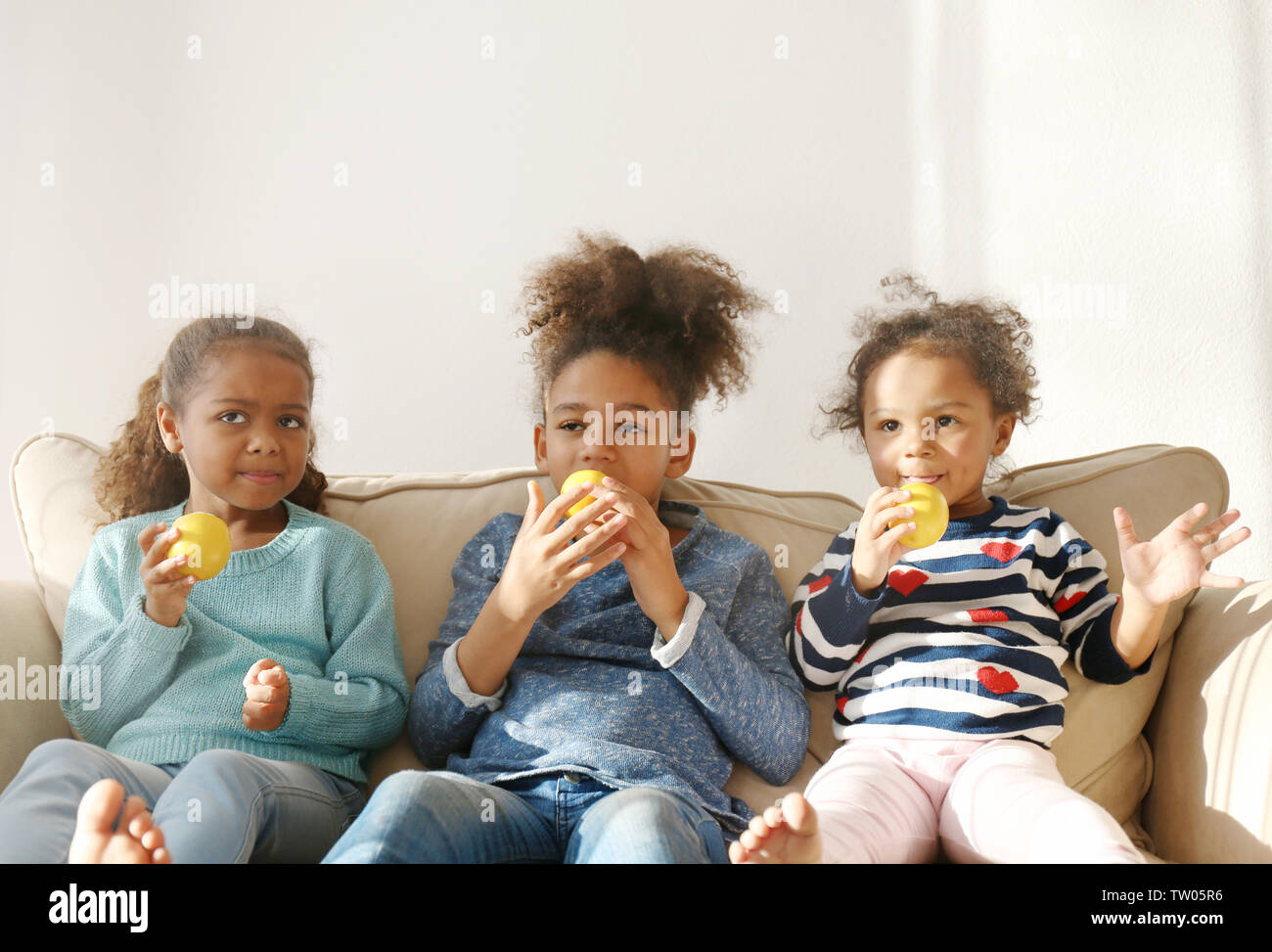 Three cute African girls sitting on sofa and eating lemons Stock Photo ...