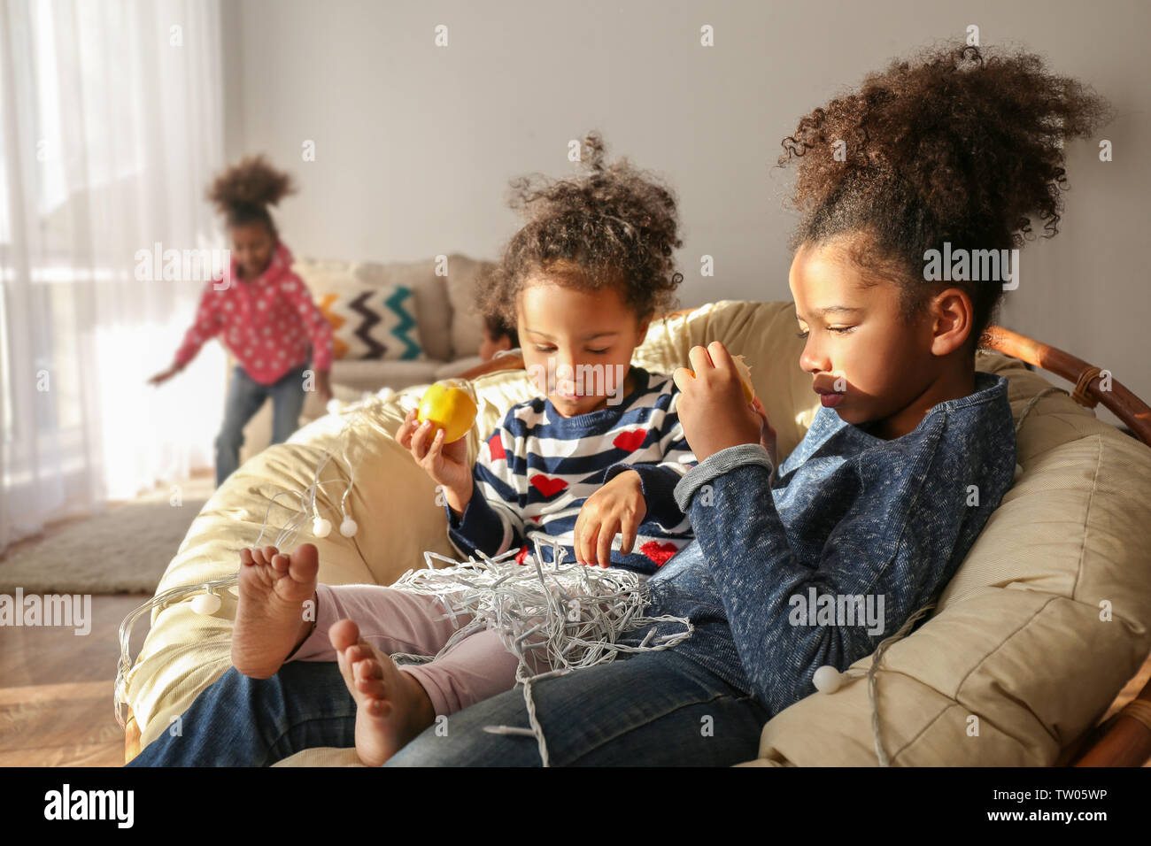 Two cute African girls sitting in armchair and eating lemons at home ...