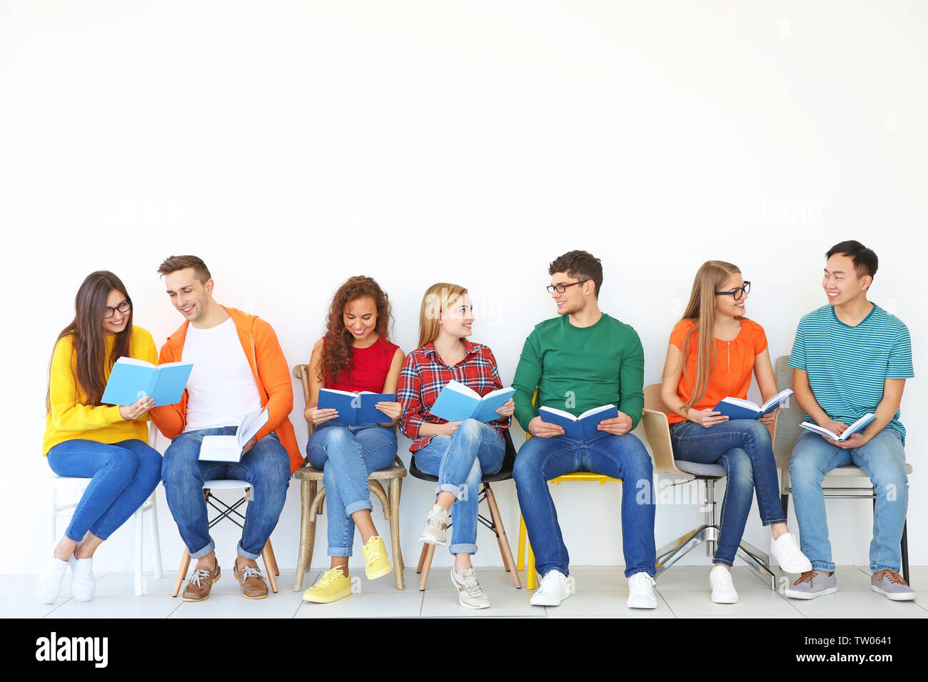 Group of people reading books while sitting near light wall Stock Photo ...