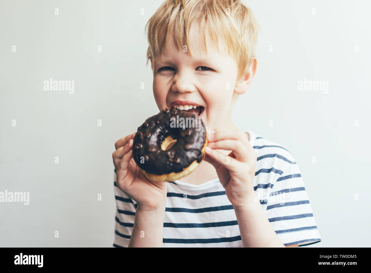A child boy eats a chocolate donut on a pure white background, real ...