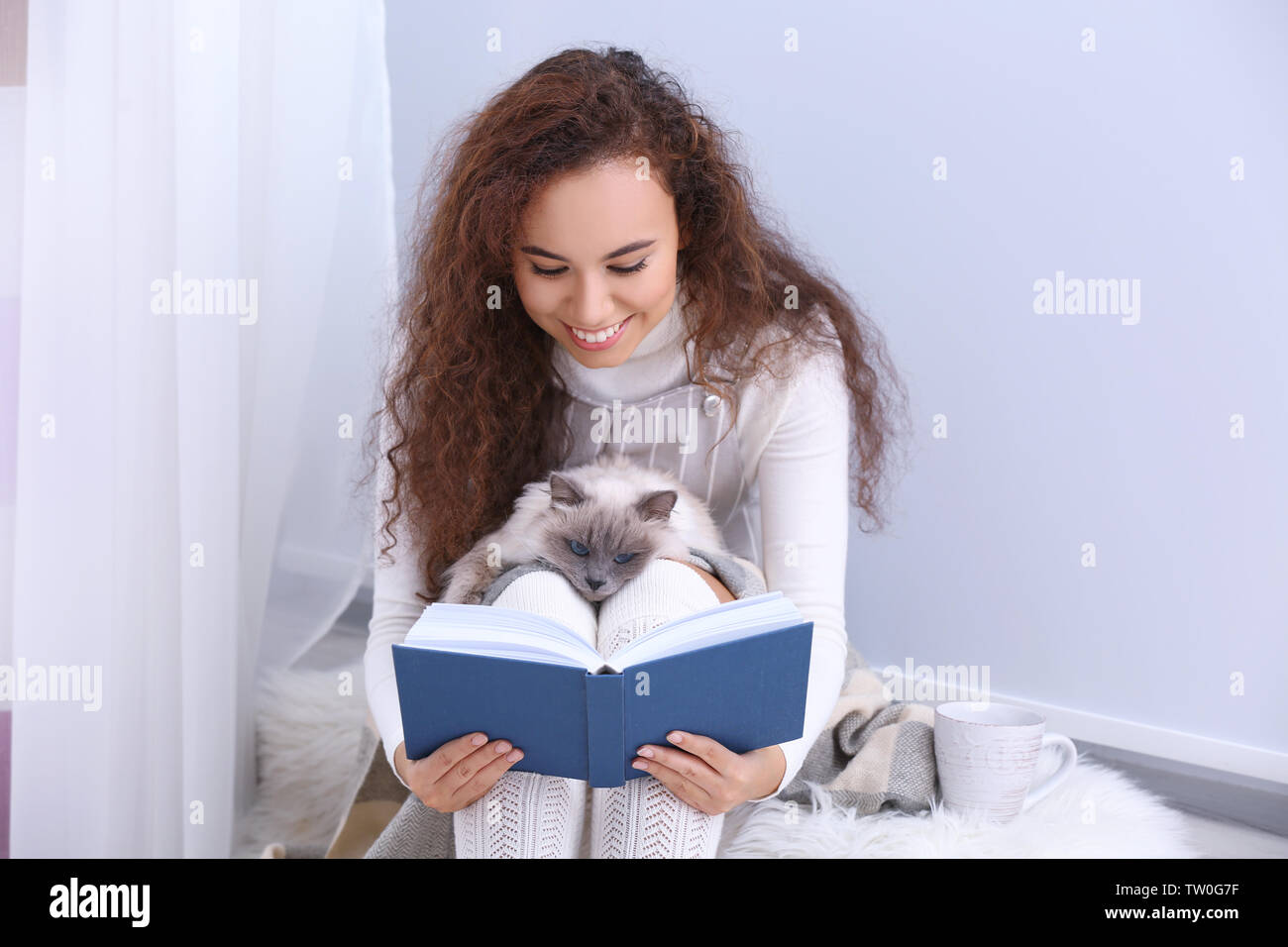 Beautiful young woman with cat on lap reading book Stock Photo - Alamy
