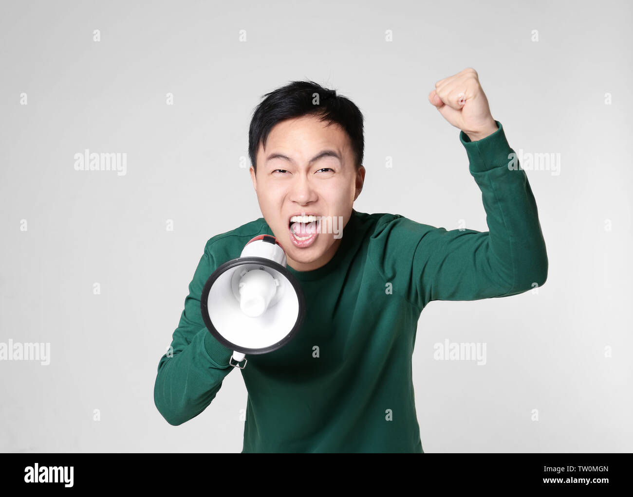 Protesting young Asian man shouting into megaphone on light background ...