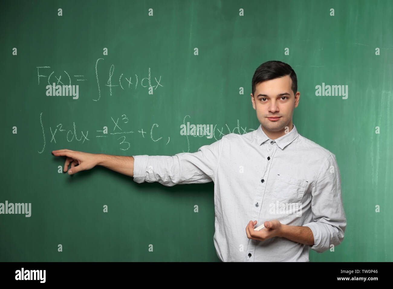 Handsome young teacher explaining math formulas written on blackboard ...