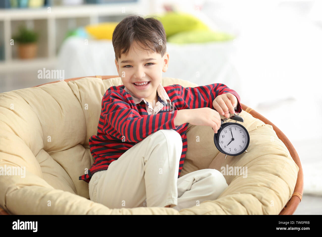 Cute little boy with alarm clock sitting on lounge at home Stock Photo ...