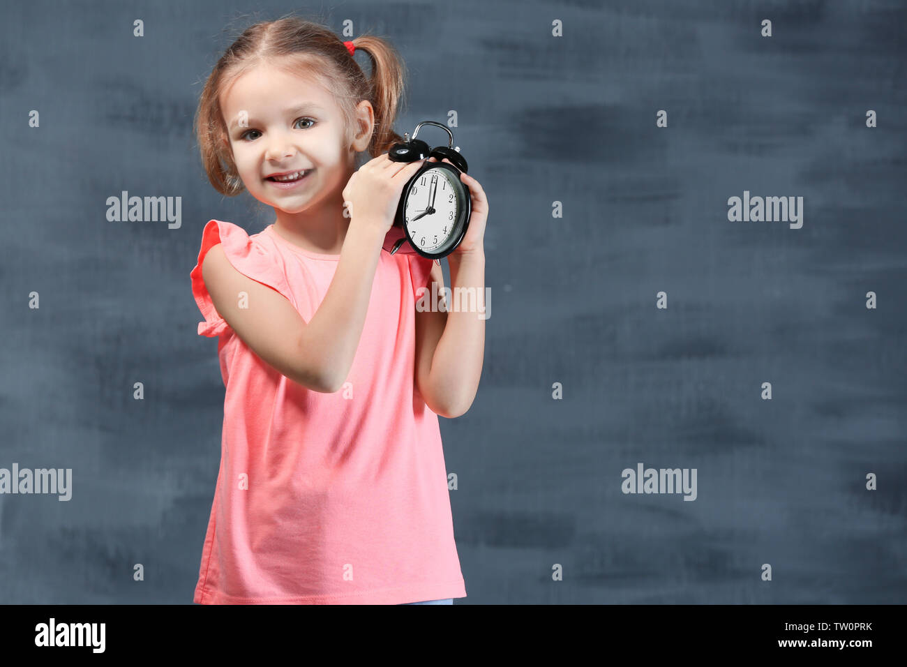 Cute little girl with alarm clock near color wall Stock Photo - Alamy