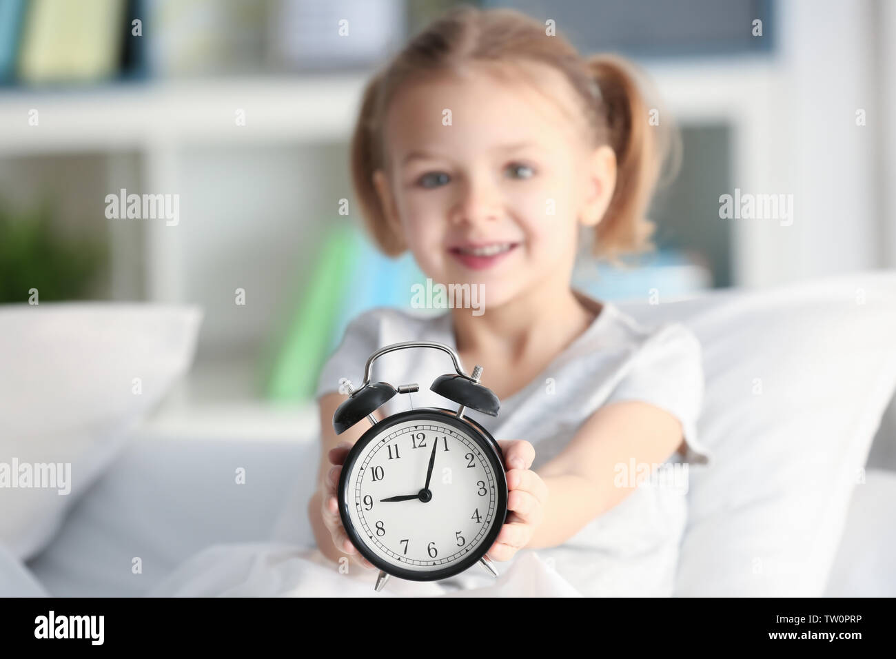 Cute little girl with alarm clock in bed Stock Photo - Alamy