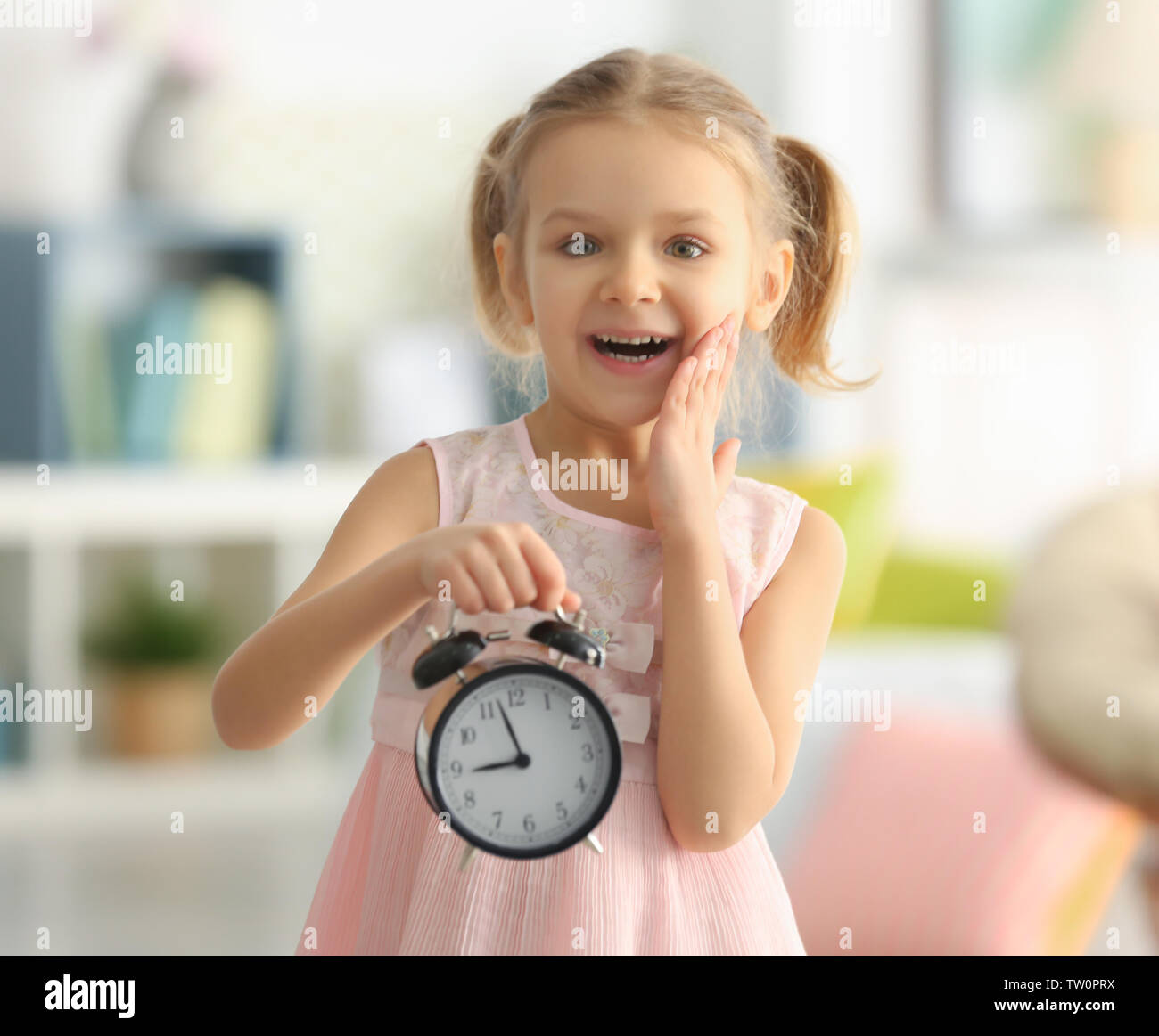 Cute little girl with alarm clock at home Stock Photo - Alamy