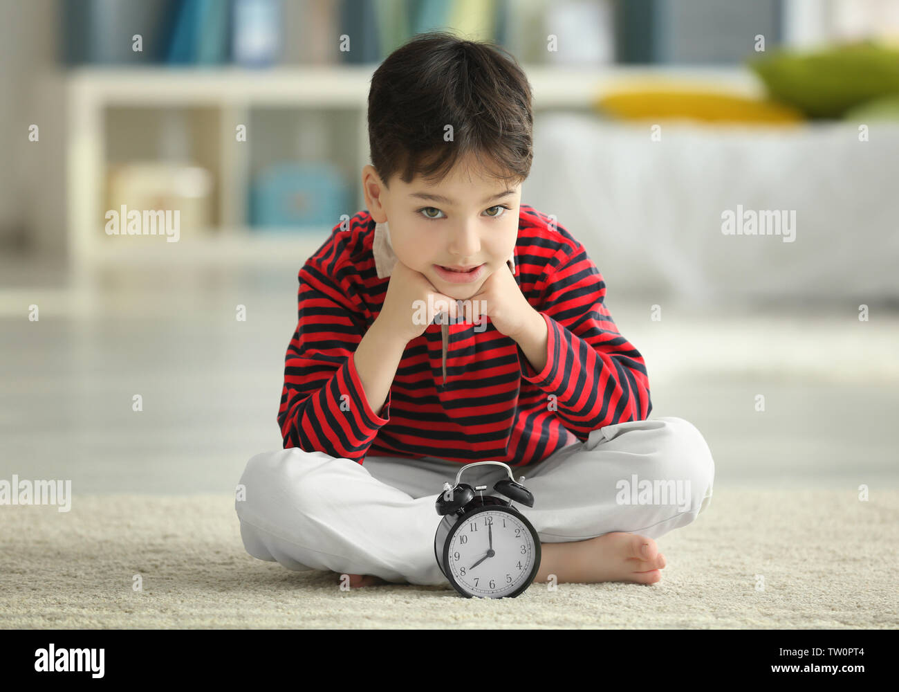 Cute little boy with alarm clock sitting on floor at home Stock Photo ...