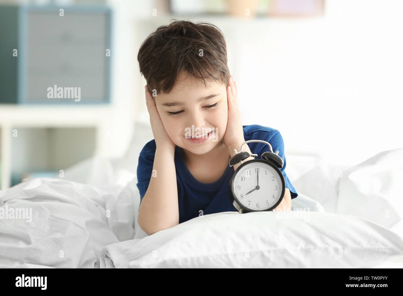 Cute little boy with ringing alarm clock in bed Stock Photo - Alamy