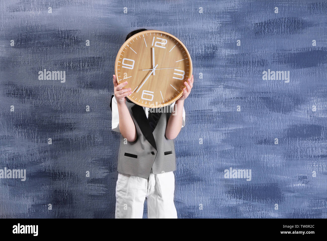 Cute little boy with big clock near color wall Stock Photo - Alamy