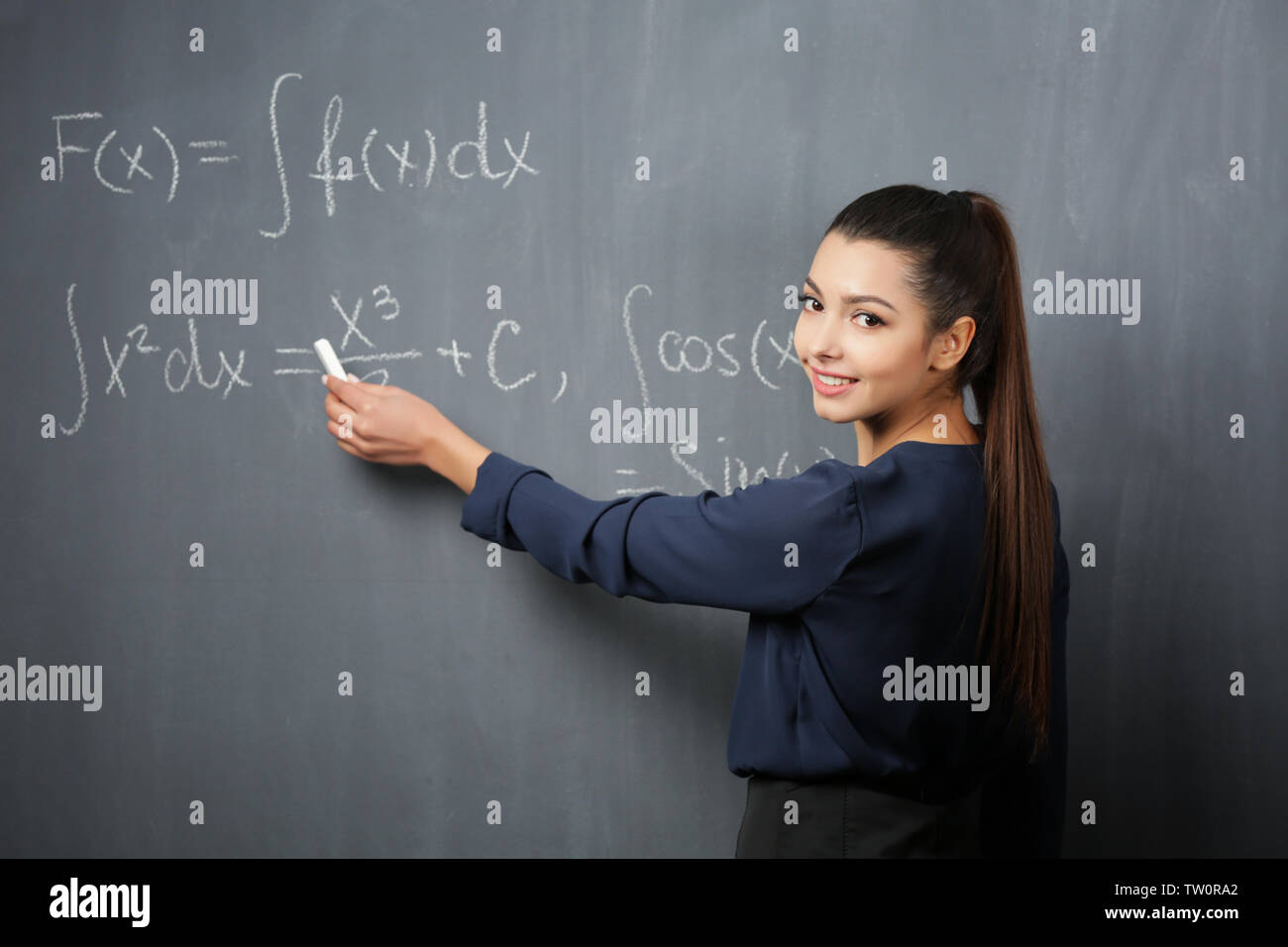 Beautiful young teacher explaining math formulas written on blackboard ...