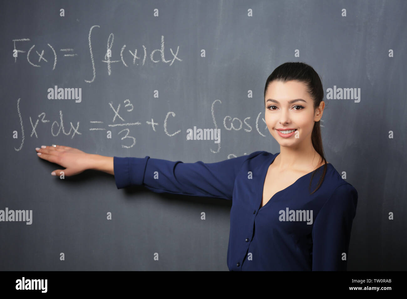Beautiful young teacher explaining math formulas written on blackboard ...