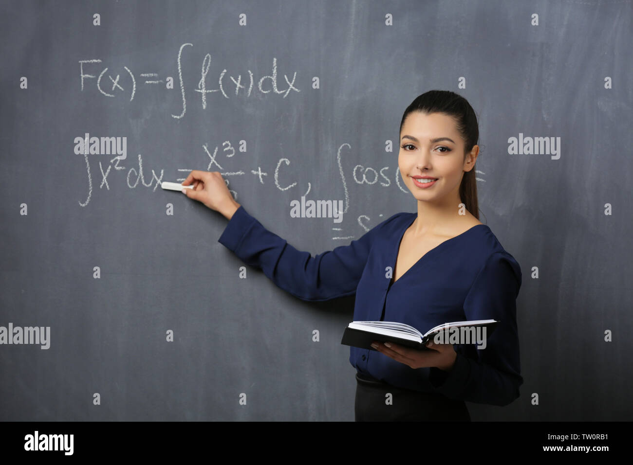 Beautiful young teacher explaining math formulas written on blackboard ...