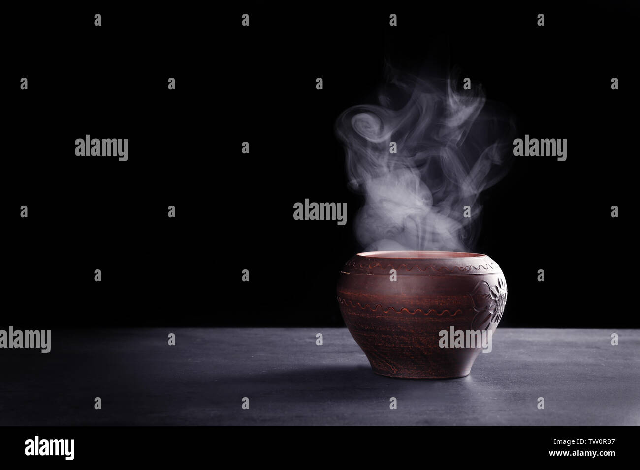 Ceramic pot with hot liquid on table against dark background Stock ...