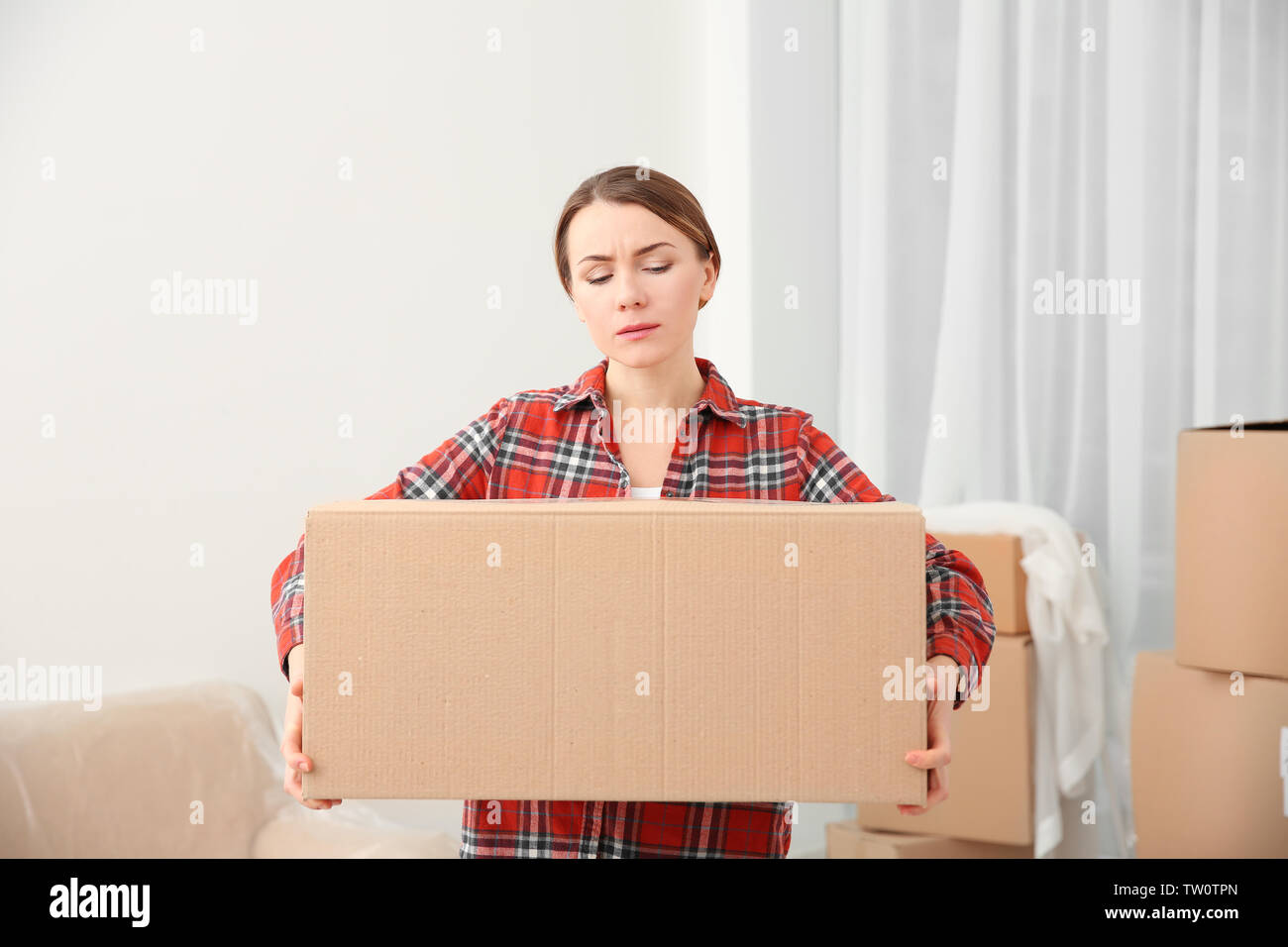 Young woman holding heavy box in room Stock Photo - Alamy