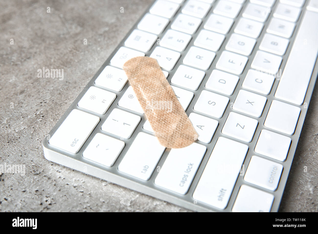 Computer keyboard with adhesive bandage on grey table Stock Photo - Alamy