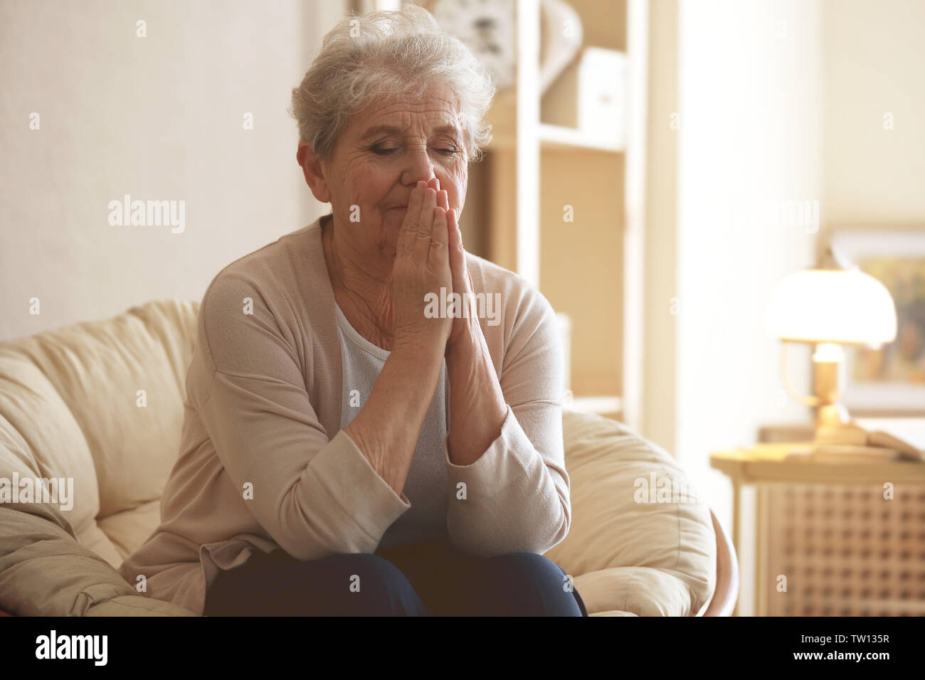 Praying elderly woman sitting on lounge at home Stock Photo - Alamy
