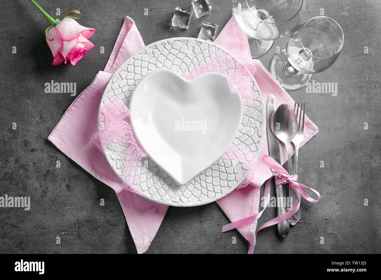 Table setting with plate in shape of heart and rose on gray background ...