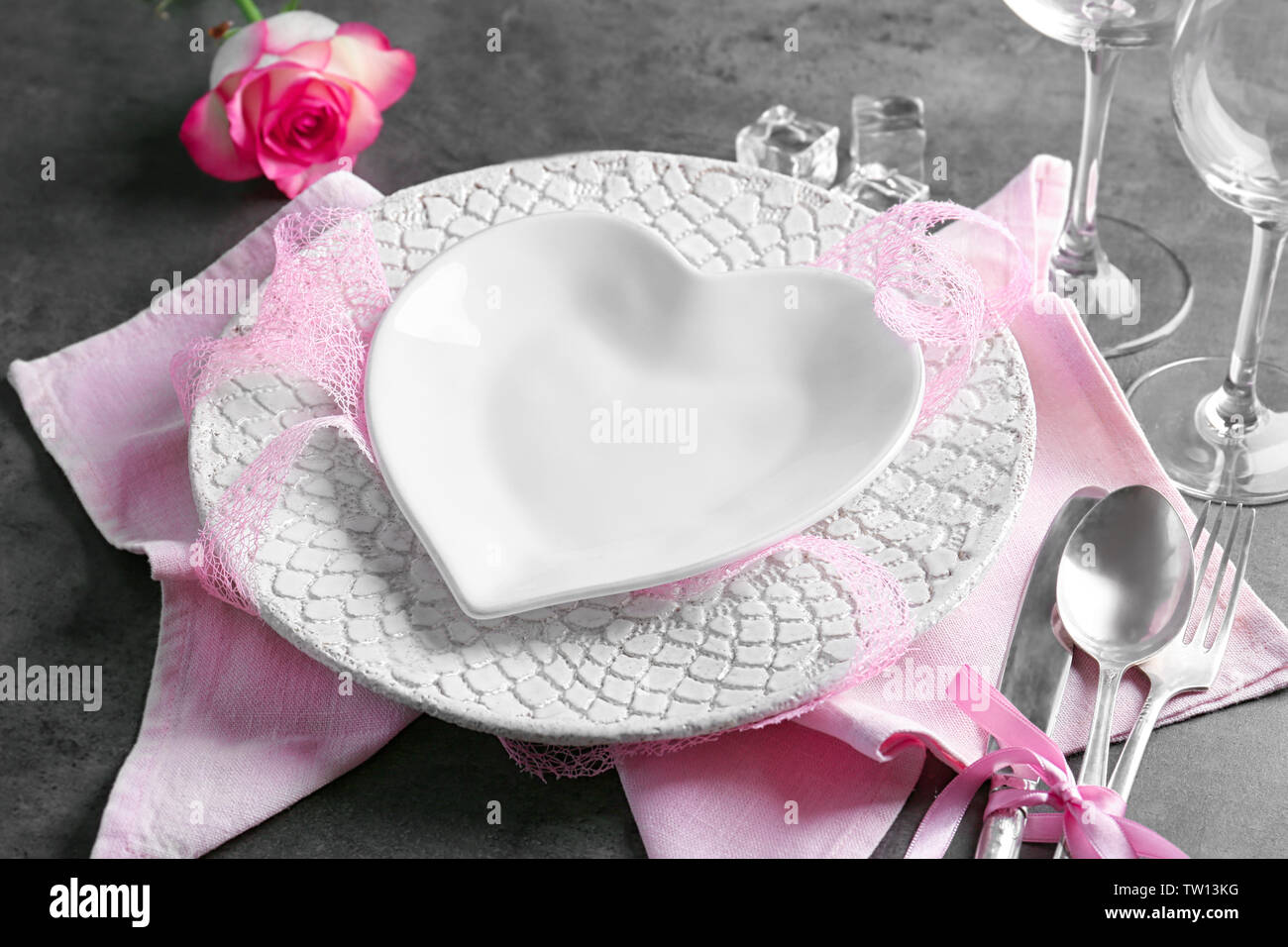 Table setting with plate in shape of heart and rose on gray background ...