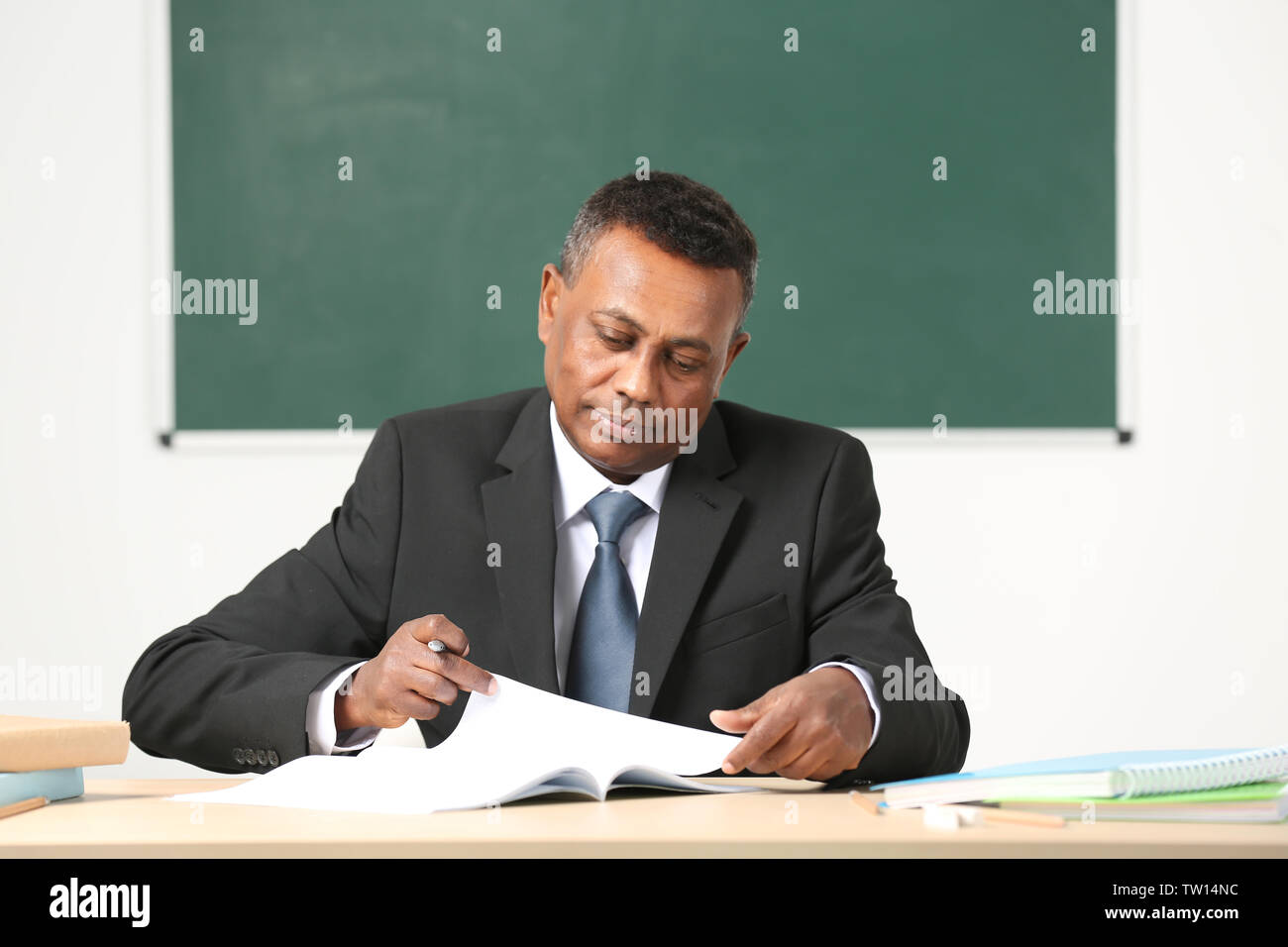 Confident Indian teacher sitting at table in classroom Stock Photo - Alamy