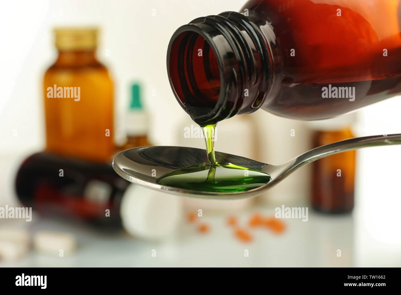 Pouring cough syrup into spoon on blurred background of medicines Stock ...