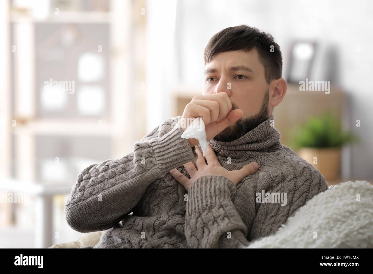 Young ill man sitting on sofa at home Stock Photo - Alamy
