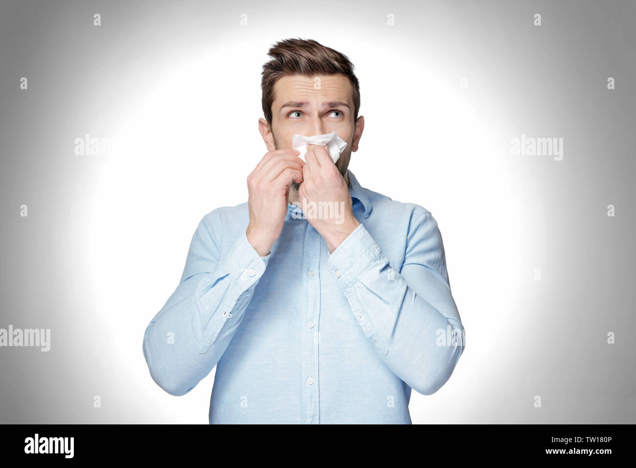 Young man using tissue to blow his nose on light background Stock Photo ...