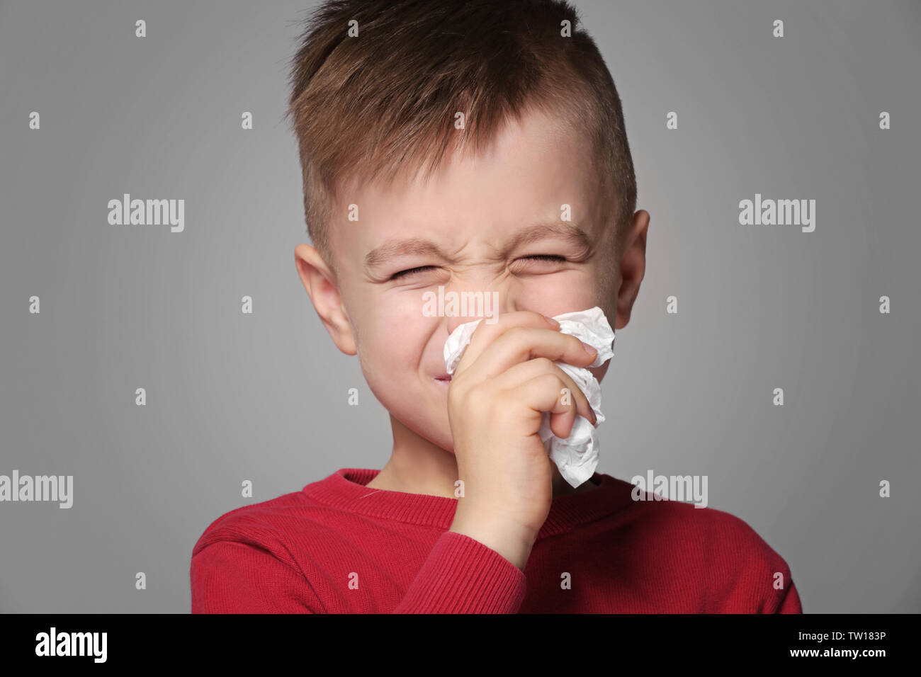 Cute little boy sneezing in tissue on gray background Stock Photo - Alamy